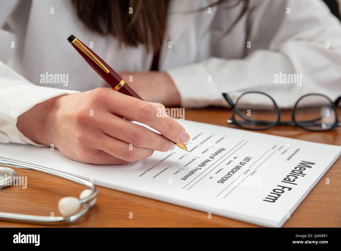 Patient medical form. Woman doctor holding a pen, close up view, wooden ...