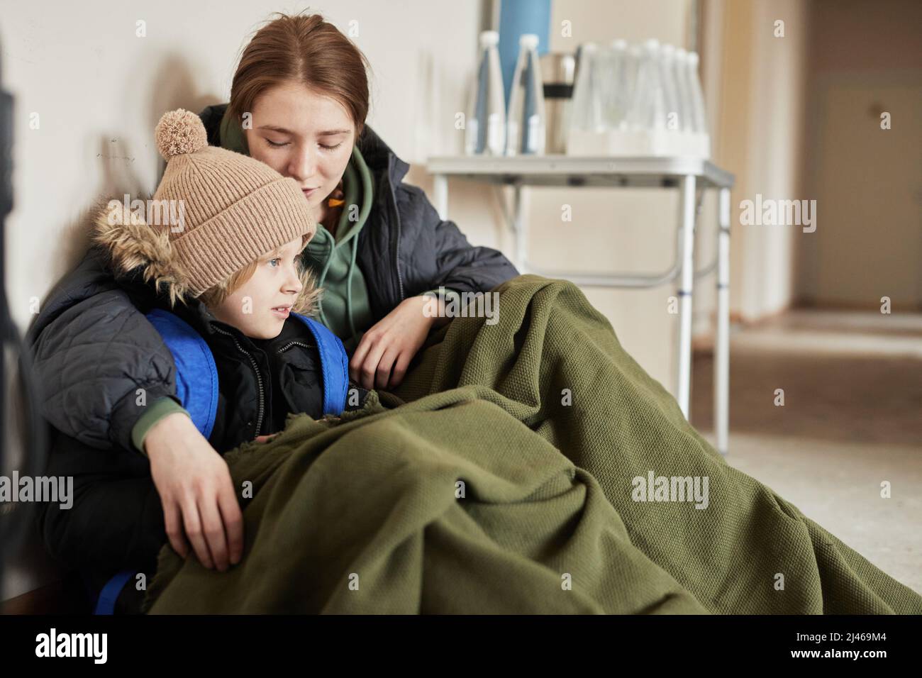 Portrait of brother and sister hiding under covers in refugee shelter ...