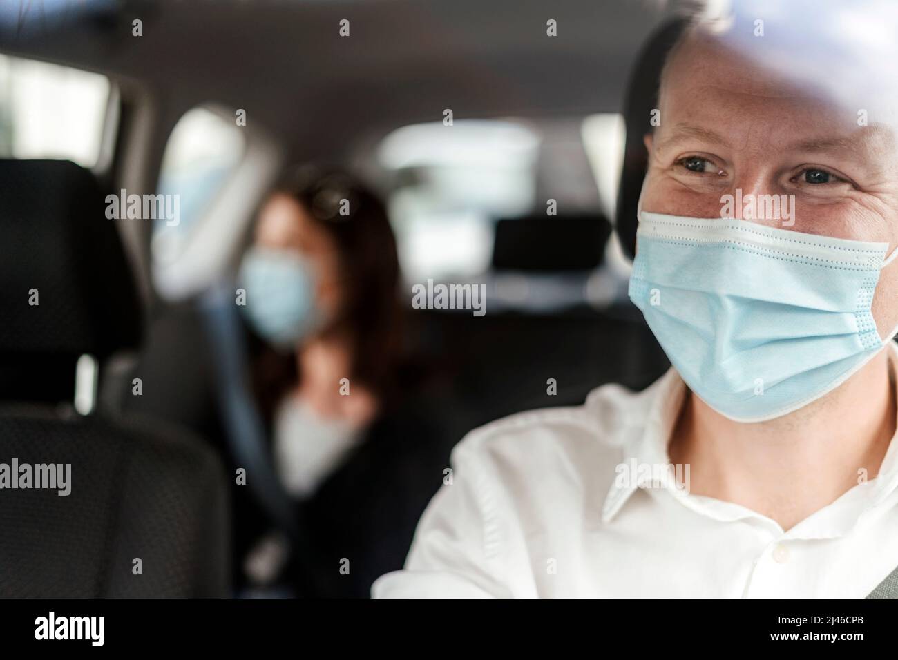 A happy taxi driver wearing a mask and the passenger on the back seat ...