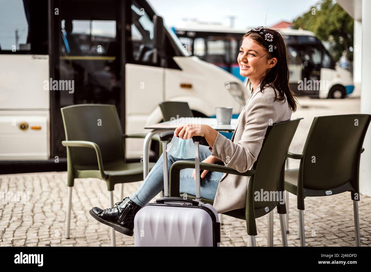 A young traveler with the luggage and protective mask sitting in the ...