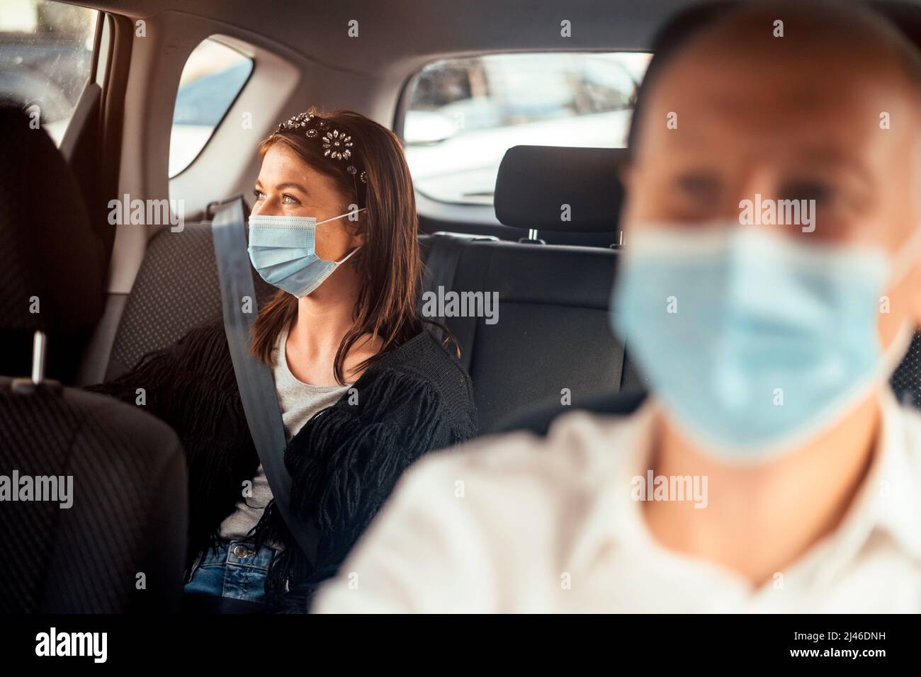 A woman wearing a protective mask sitting on the back seat of a taxi ...