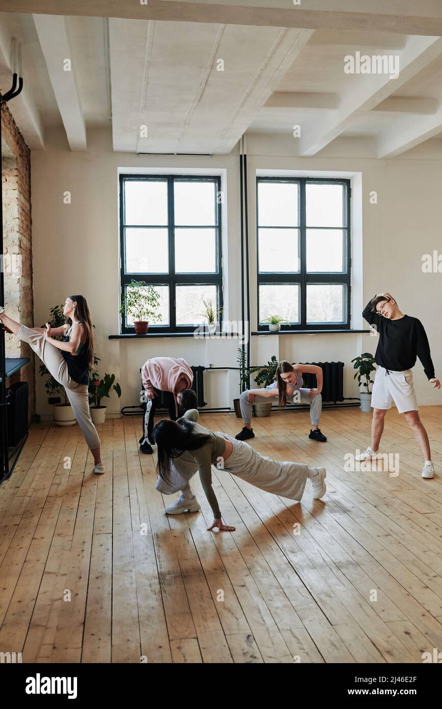 Group of adolescent people in activewear doing warmup exercises on ...