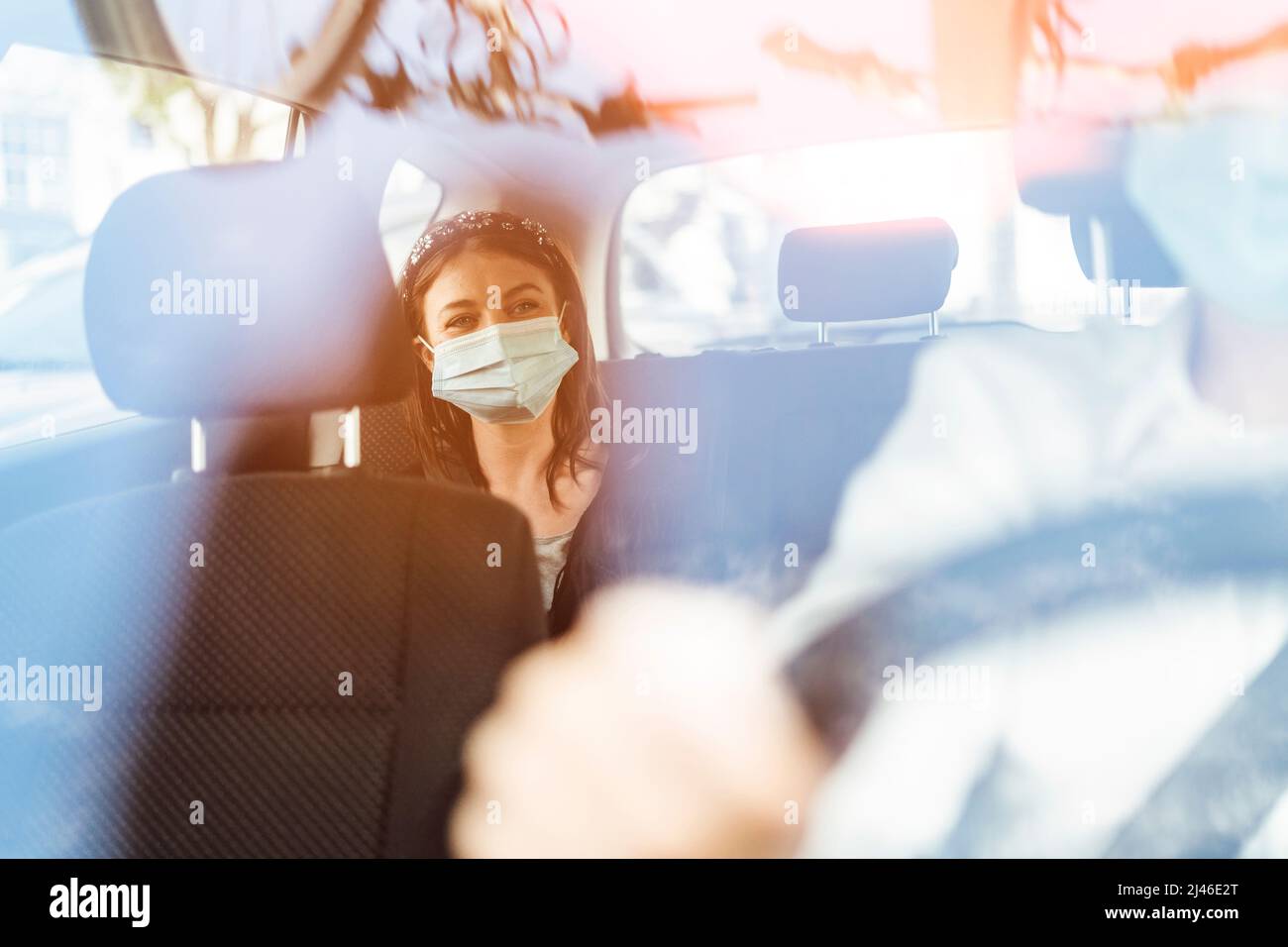 A woman wearing a protective mask sitting on the back seat of a taxi ...