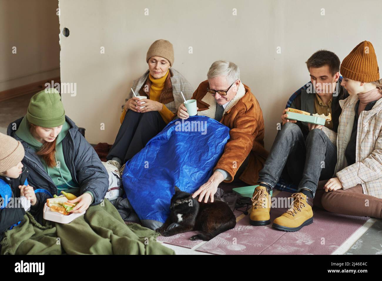 Group of Caucasian refugees eating food while hiding in shelter on ...