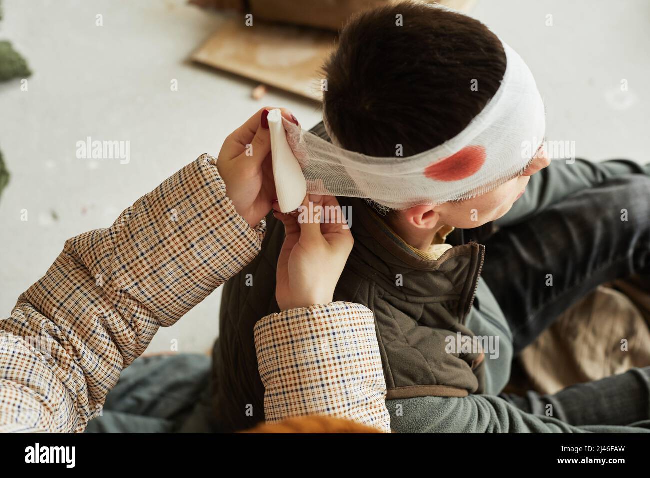 High angle of nurse bandaging head of wounded civilian man in refugee ...