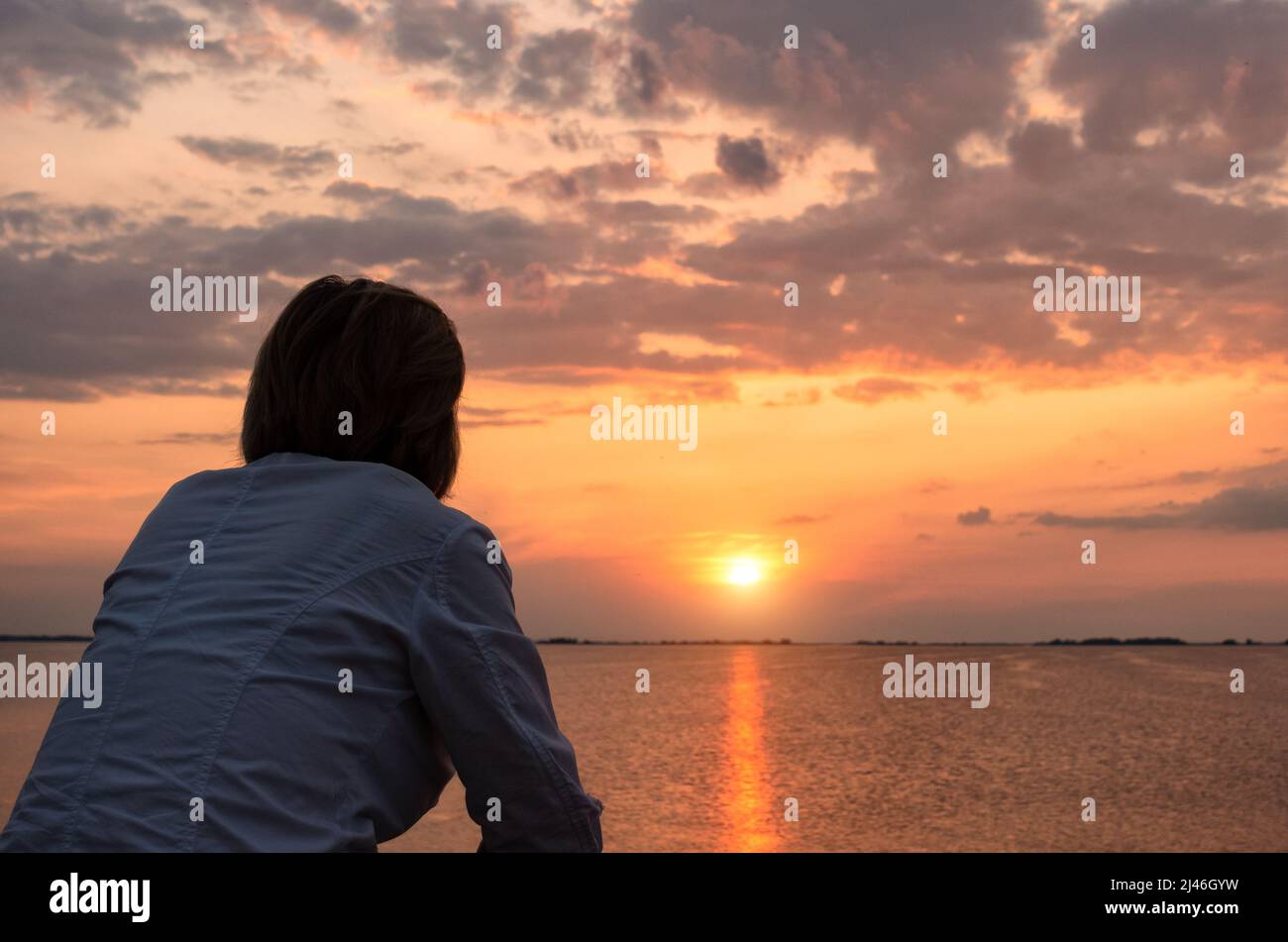 Girl sitting by the sea on a sunset background Stock Photo - Alamy