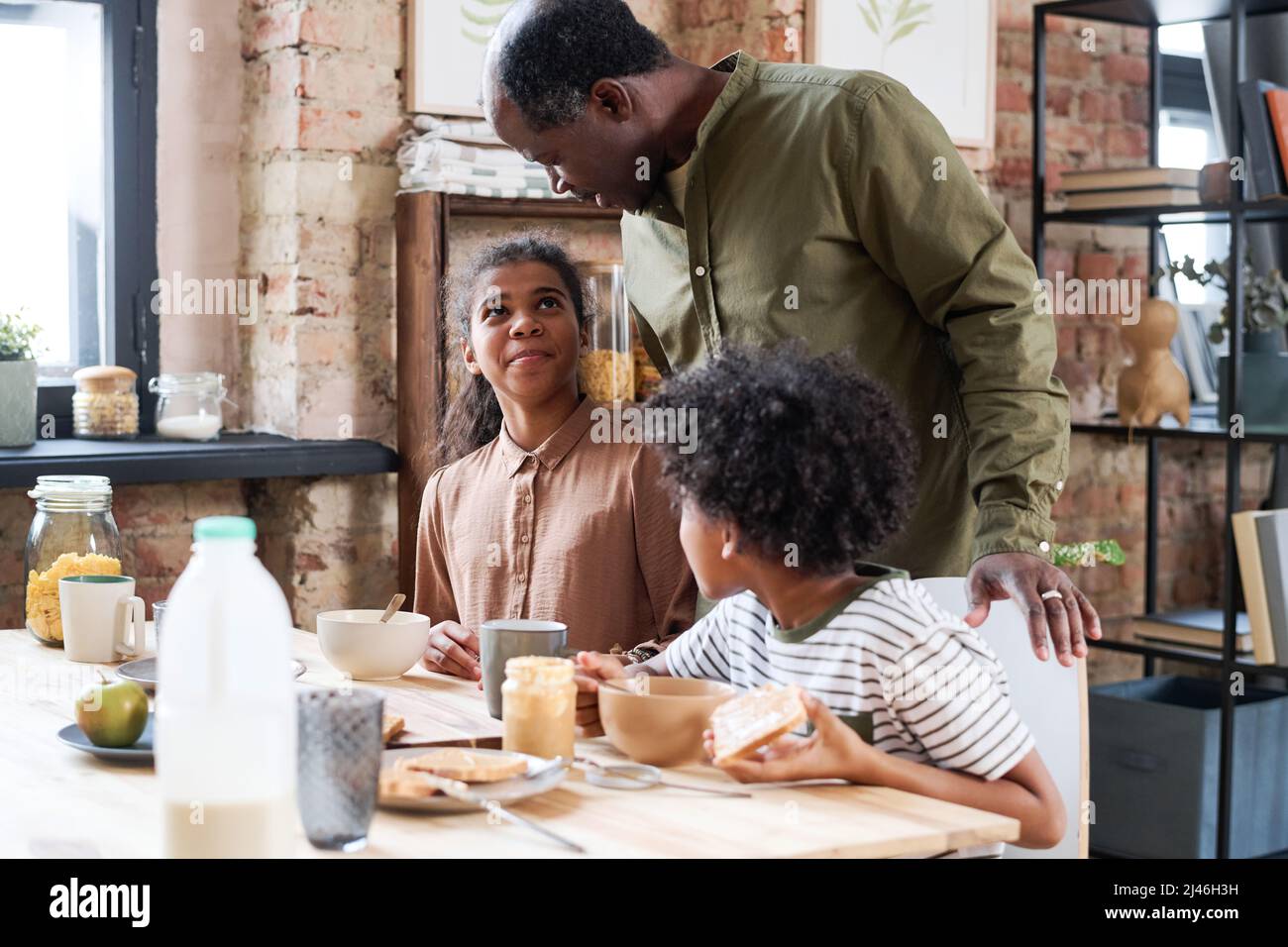 Senior African American man bending over his grandchildren at breakfast ...