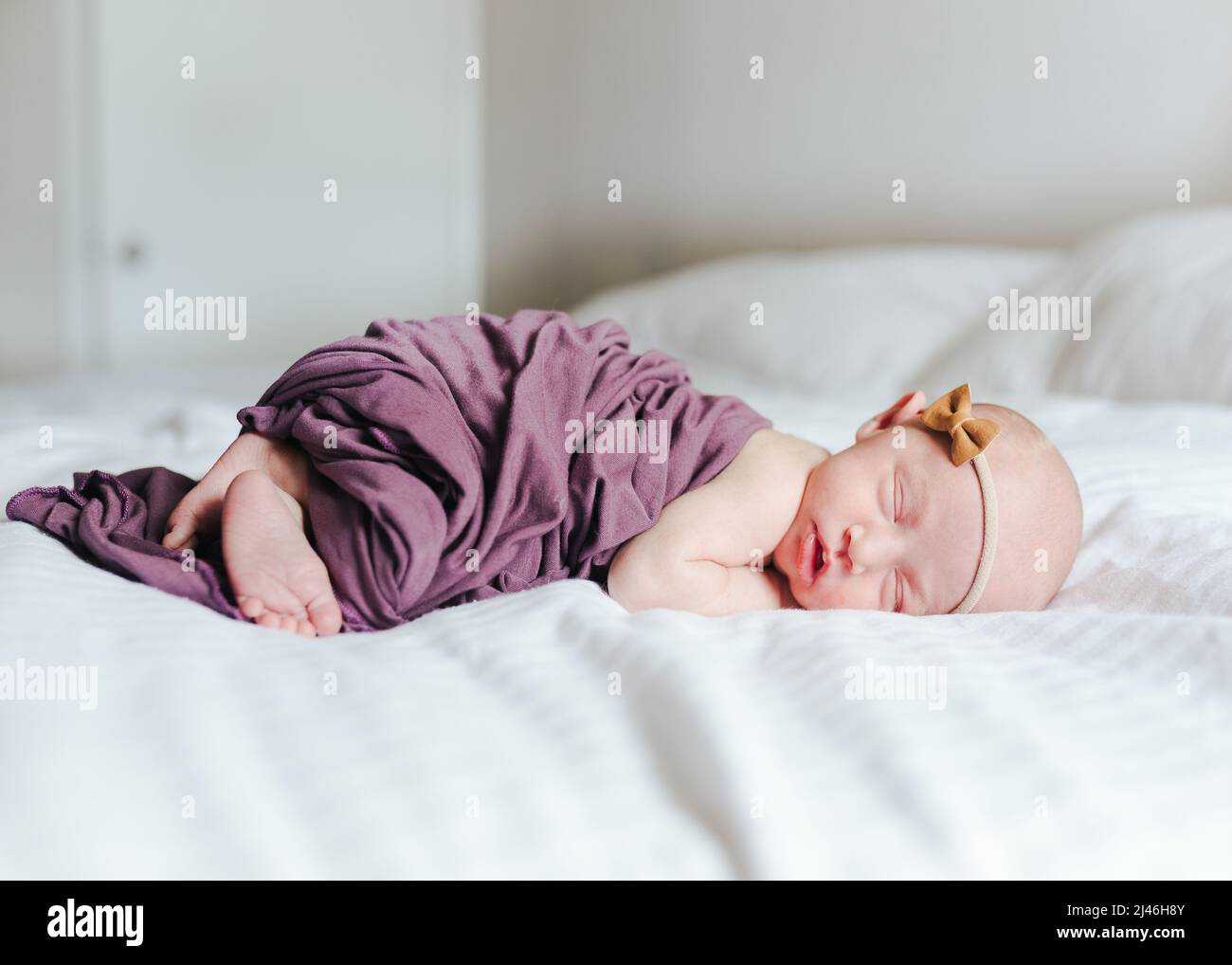 newborn baby girl covered in a swaddle laying on a white bed Stock ...