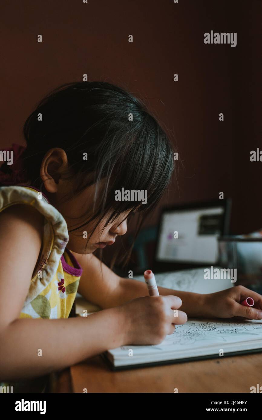 Preschooler coloring at home with laptop open Stock Photo - Alamy