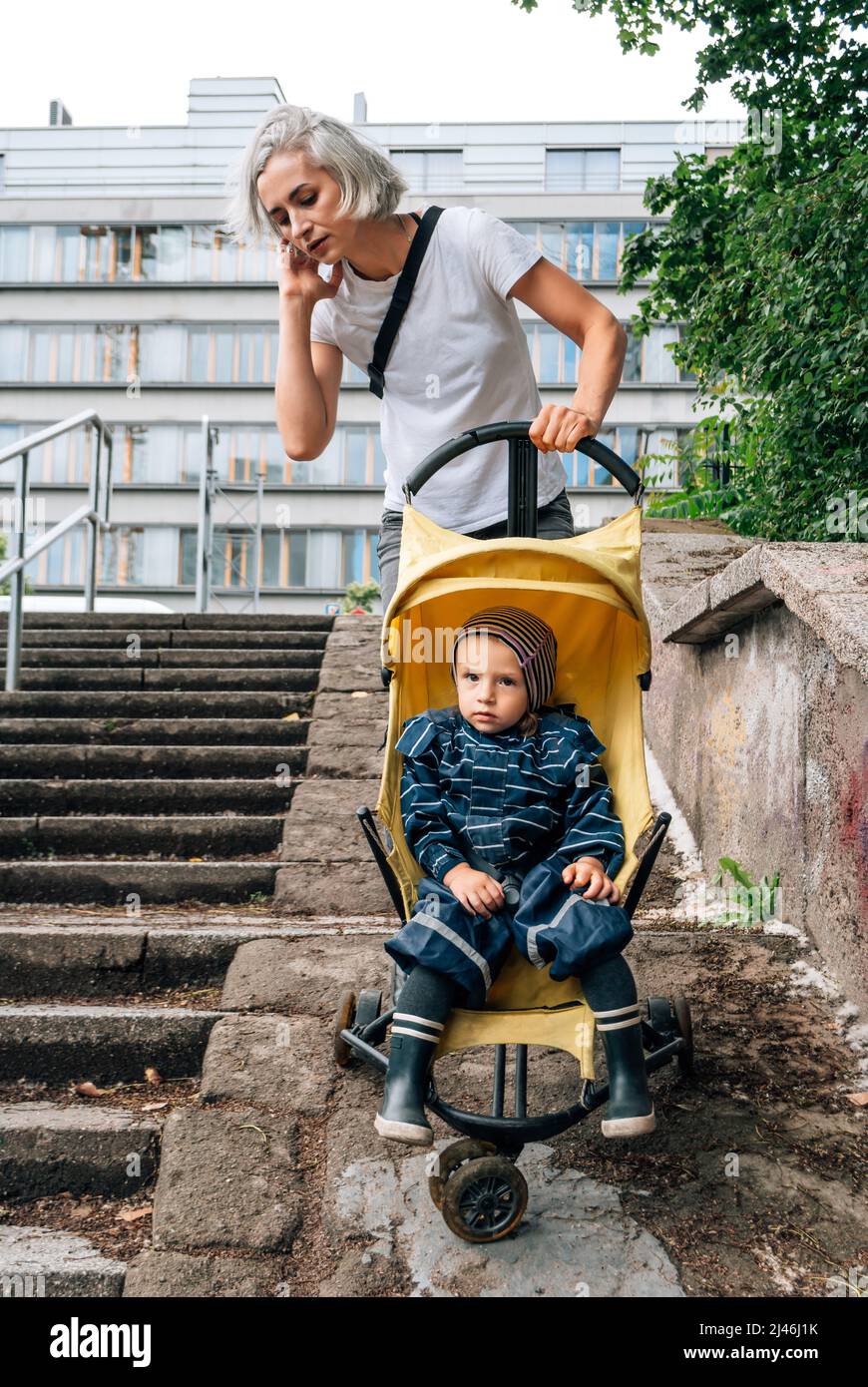 A mother uses a ramp to roll down a stroller with her young son Stock ...