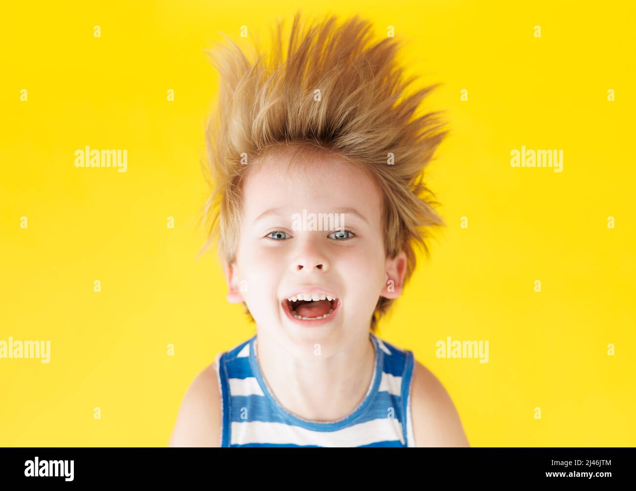 Happy child shouting against yellow paper background. Funny kid hanging ...