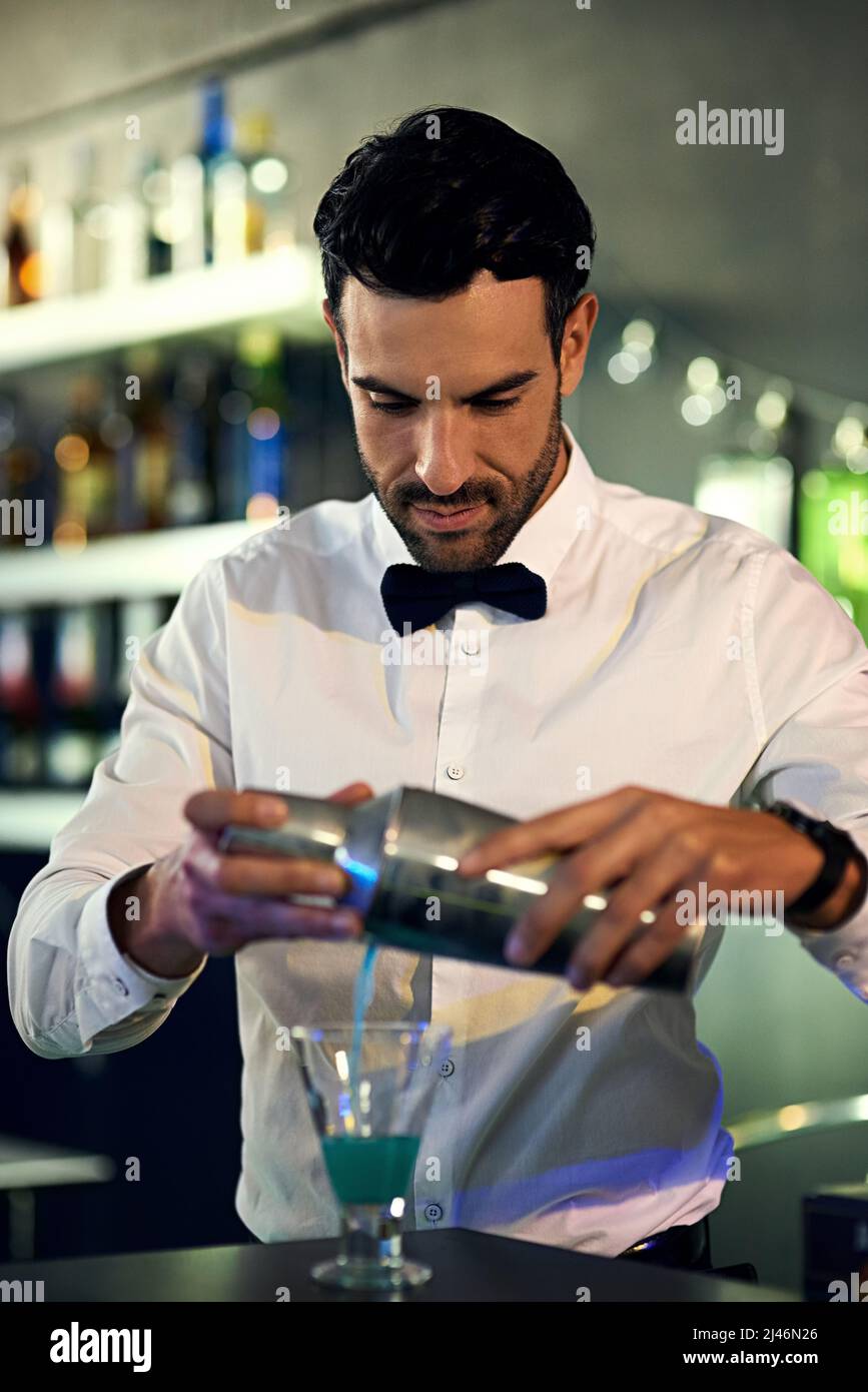 How to make the perfect cocktail. Shot of a barman mixing drinks behind ...