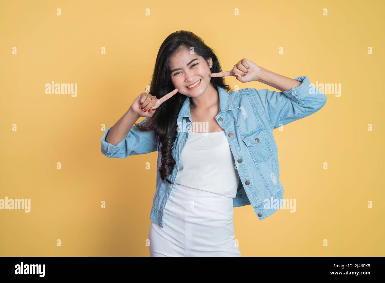 Smiling cute young woman with two fingers pointing to cheek Stock Photo ...
