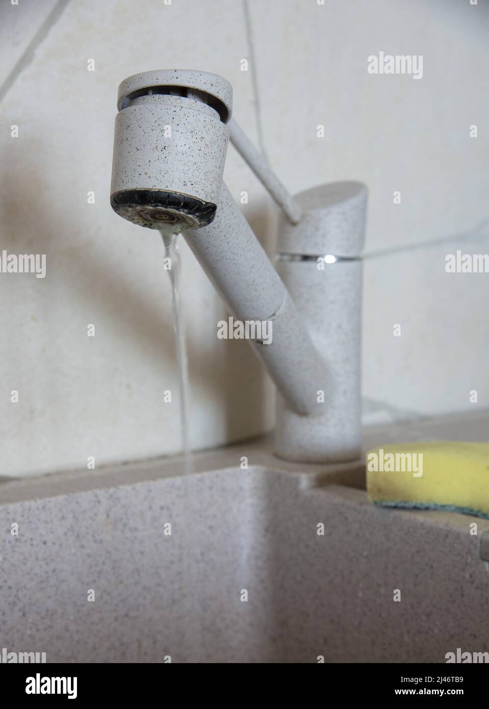 Ceramic beige kitchen faucet over a stone sink. An old dish sponge next ...