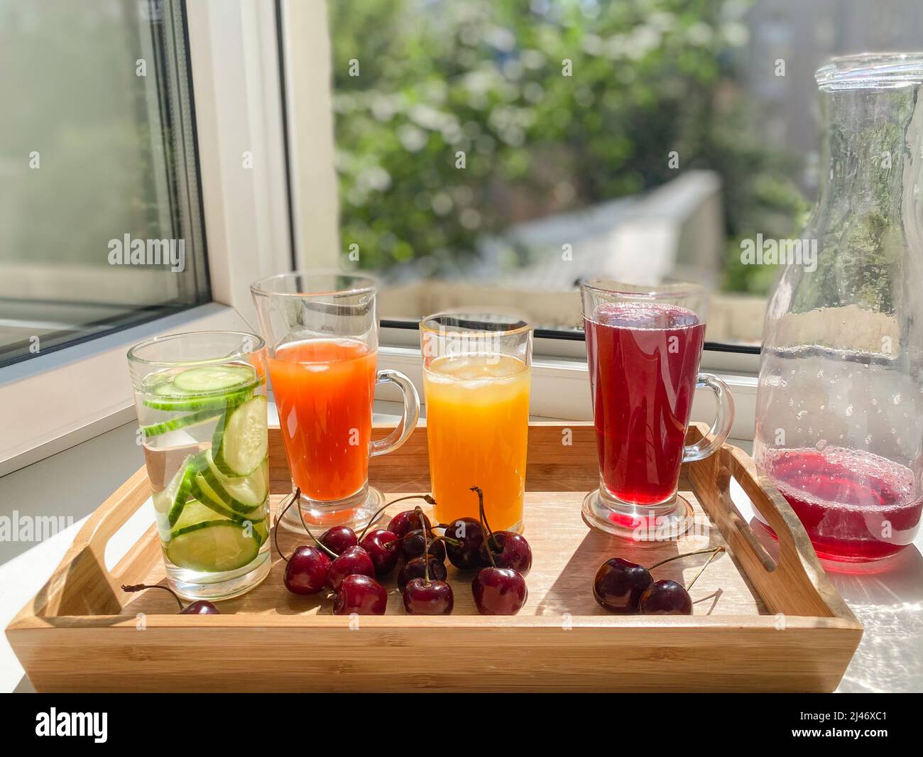 Wooden tray with colorful drinks, cherries on a windowsill. Decanter ...