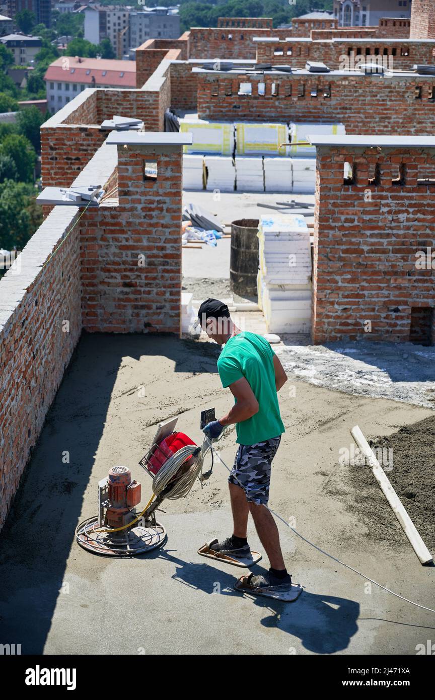 Man builder using troweling machine while screeding floor on the roof ...