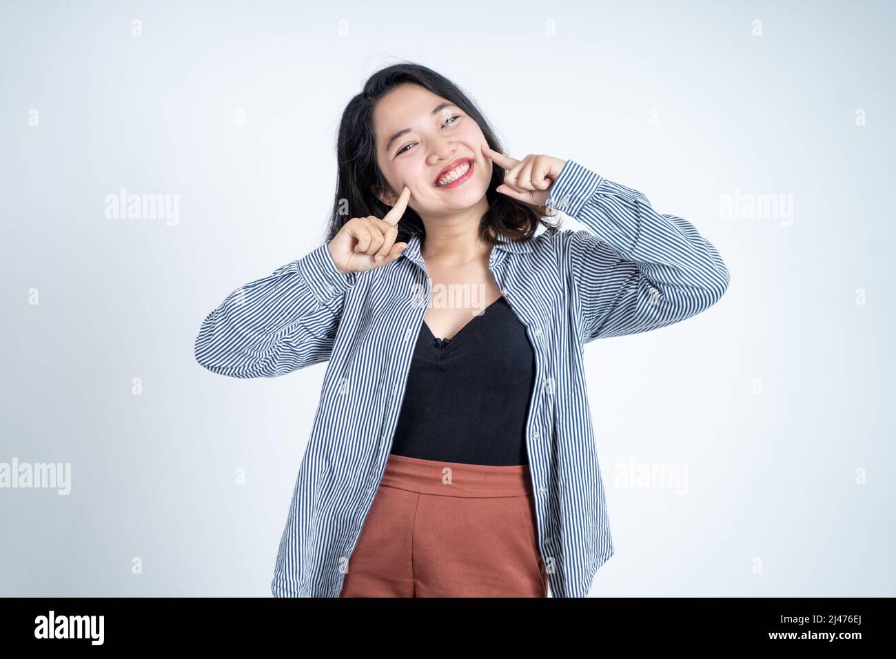 Smiling young woman standing with two fingers pointing to cheek Stock ...