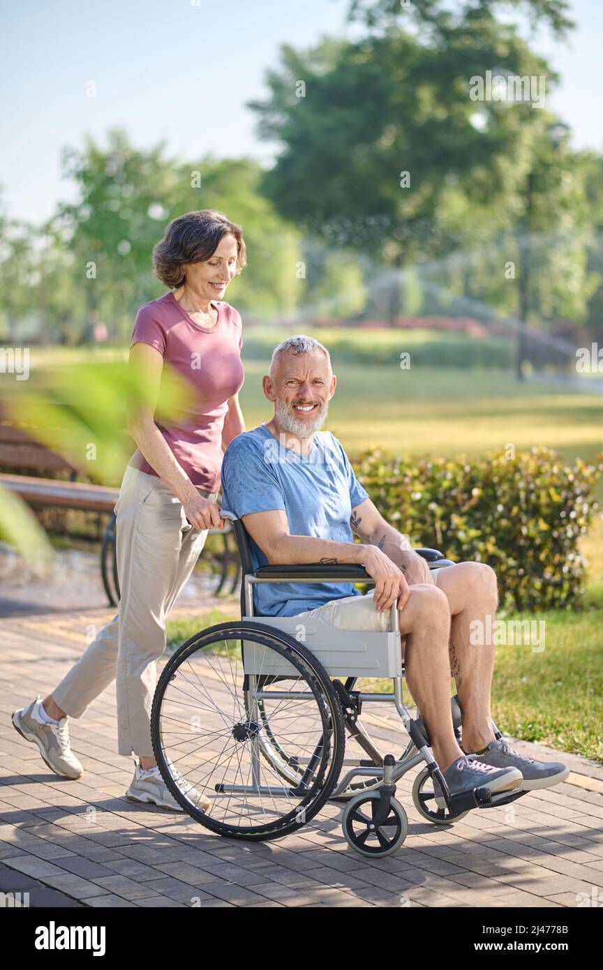 A dark-haired woman carrying her husband in a wheel chair Stock Photo ...