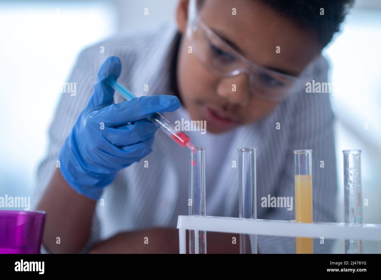 A dark-haired boy in a lab coat holding a syringe with a reagent and ...