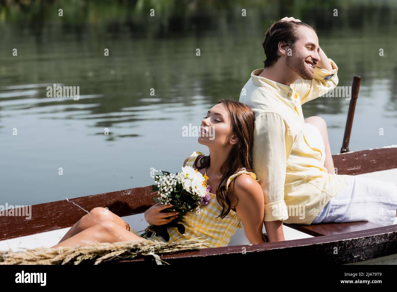happy young woman holding flowers and leaning on back of smiling ...
