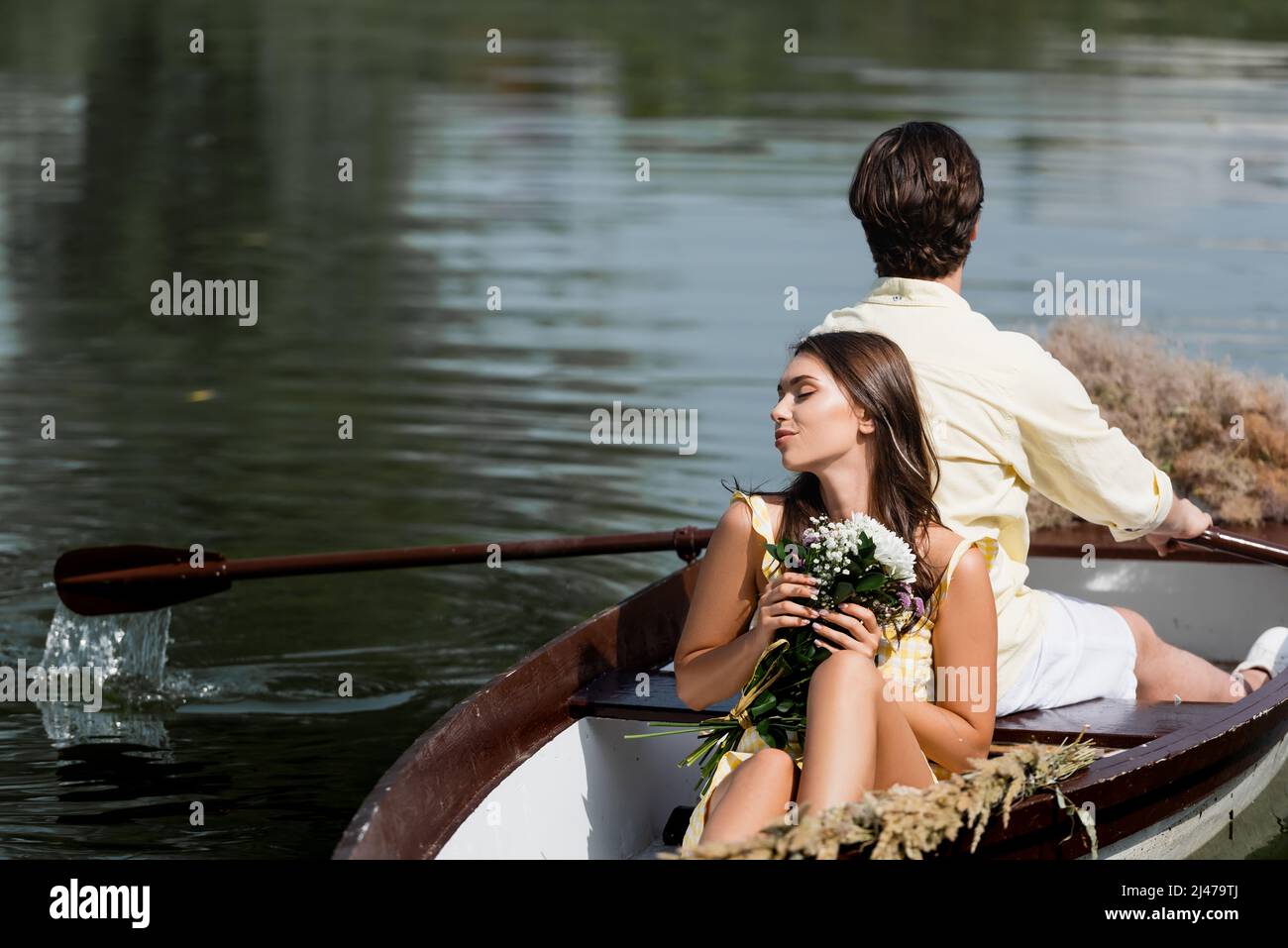 young woman holding flowers and leaning on back of man during romantic ...