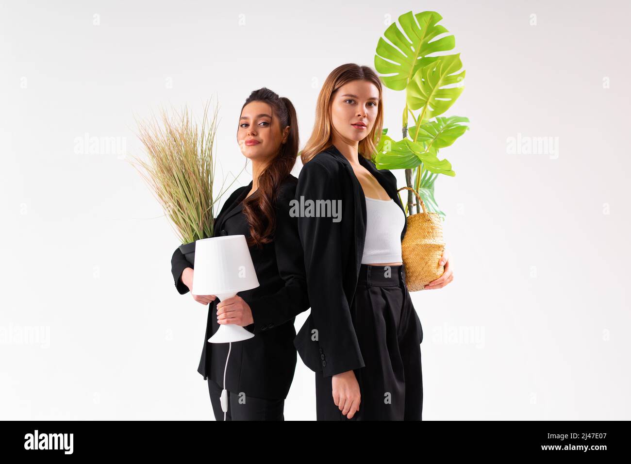 Two business woman dressed black suit holding houseplant and lamp ...