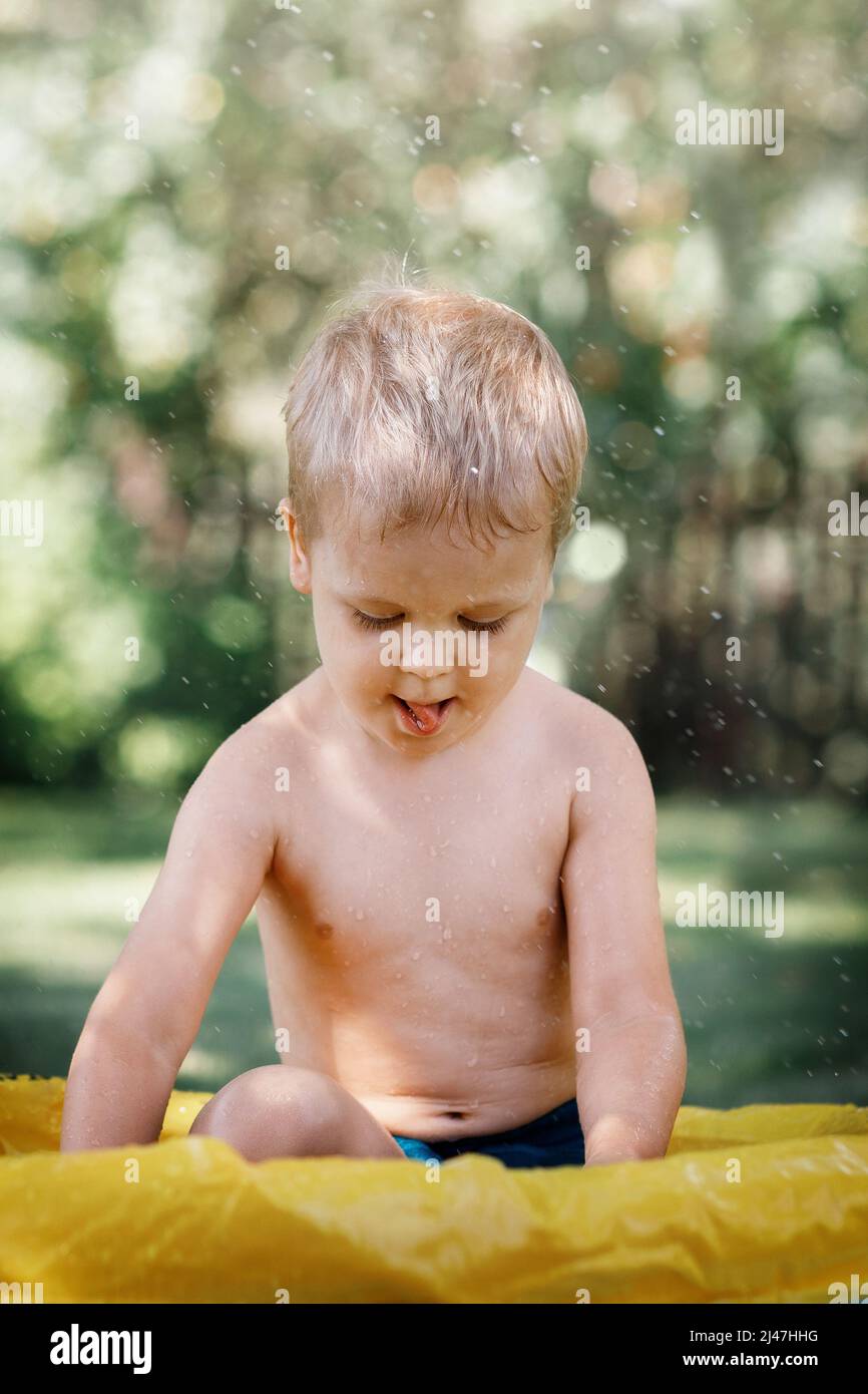 Baby boy concentrated plays at pool in the garden. Showing his tongue ...