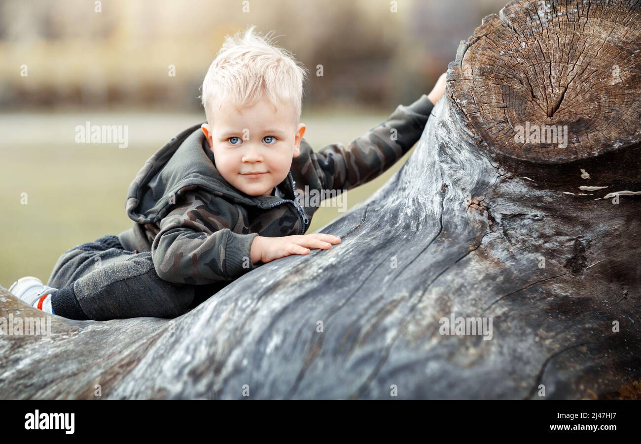 Agile boy climb over big branch. Cautiously looking at camera like ...