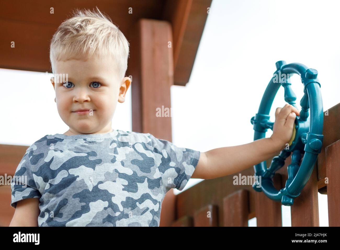 Pleased child is beeping a ship wheel in a playground. Kid wearing ...
