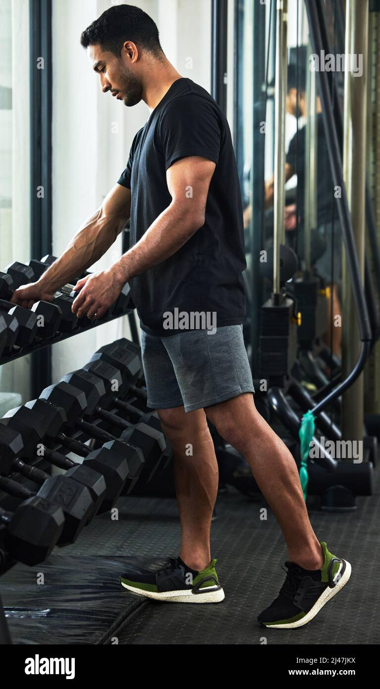 Its time to lift some weights. Shot of a man picking up dumbbells at ...