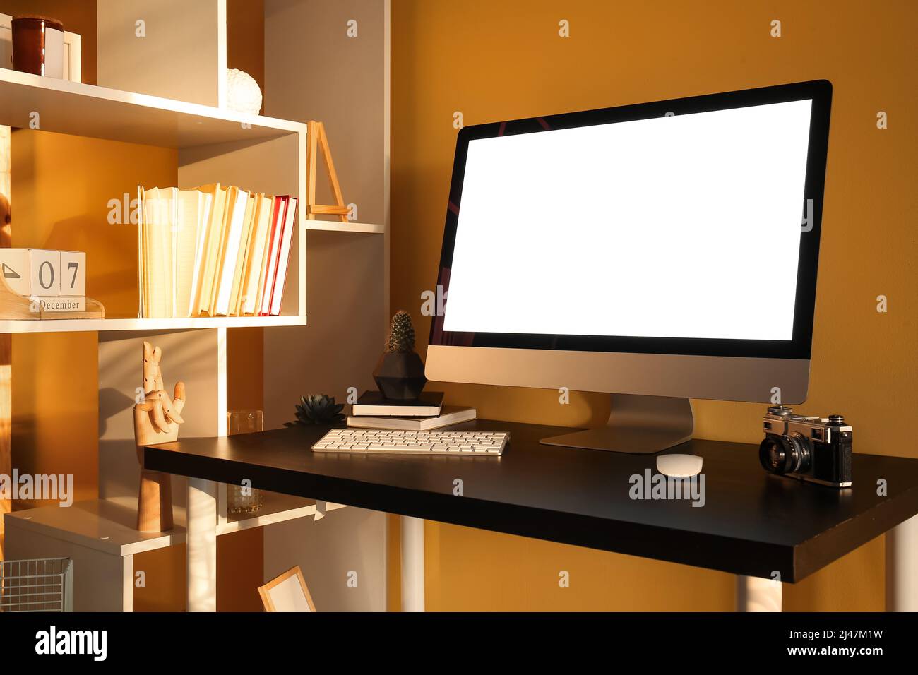 Comfortable workplace with computer and shelf unit with books near ...