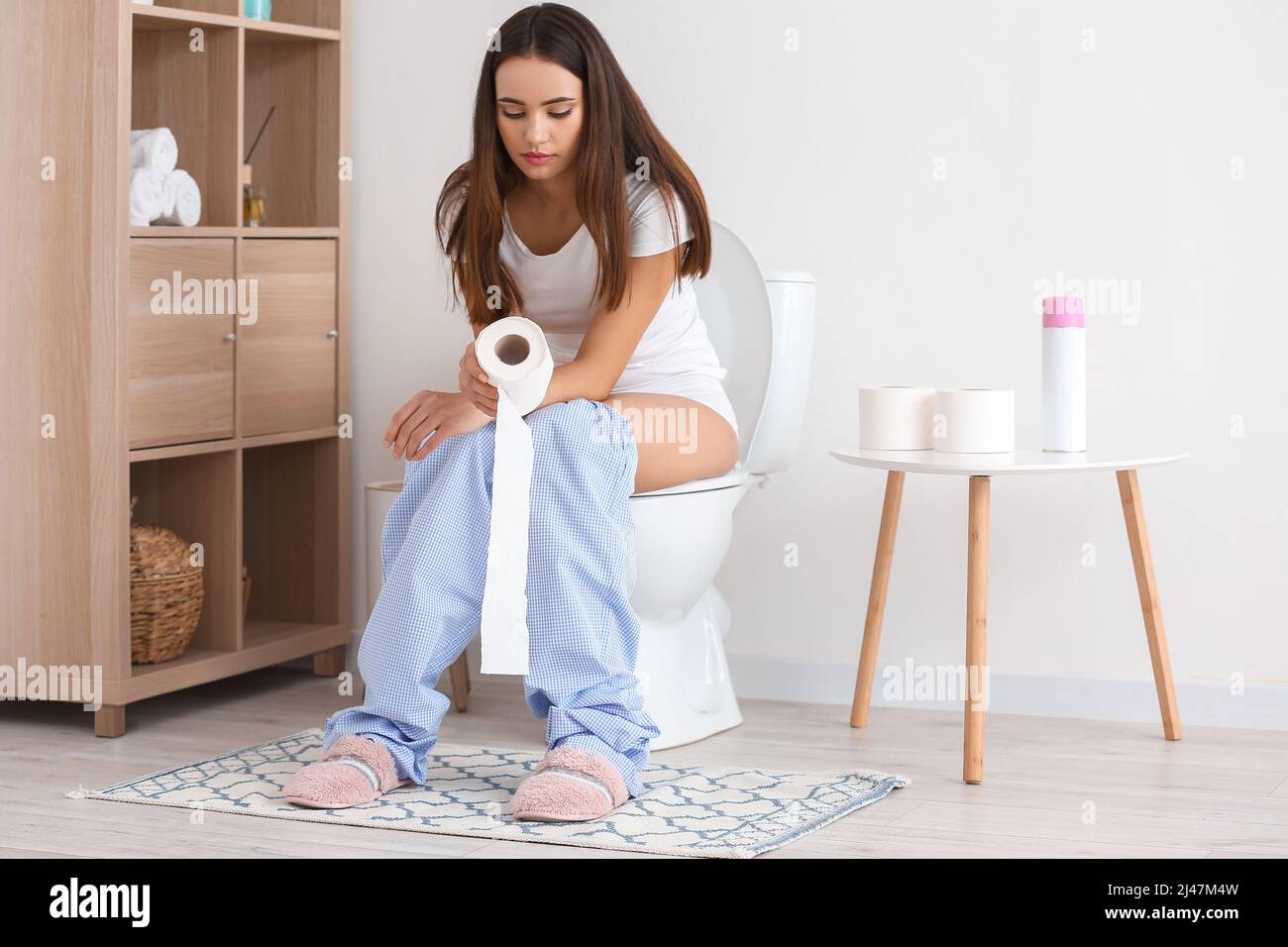 Young woman with paper roll sitting on toilet bowl in restroom Stock ...