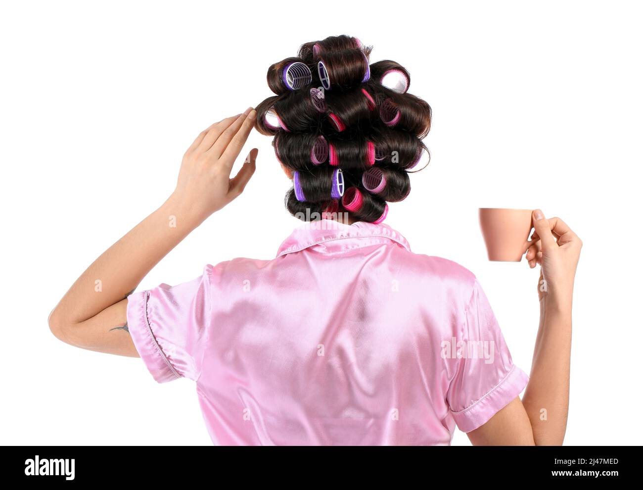 Beautiful young woman in pajamas and hair curlers drinking coffee on ...