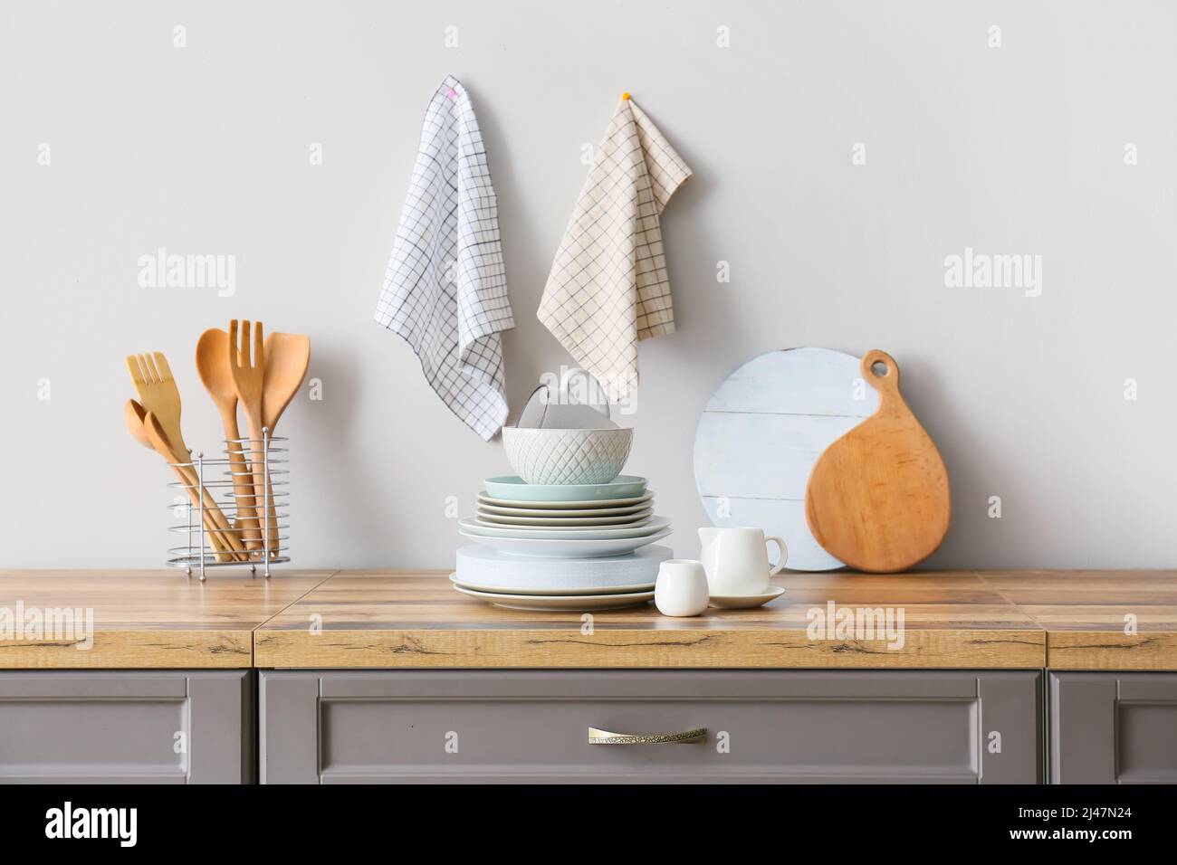 Beautiful dinnerware and kitchen utensils on counter near light wall ...