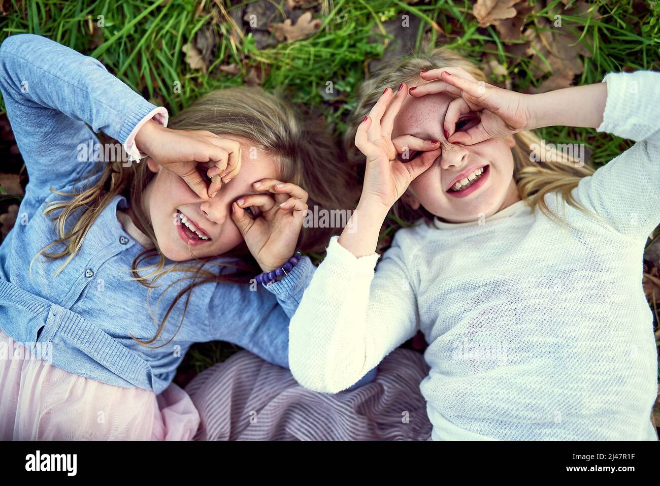 Everything is fun when youre young. Portrait of two little sisters lying on the grass outside ...