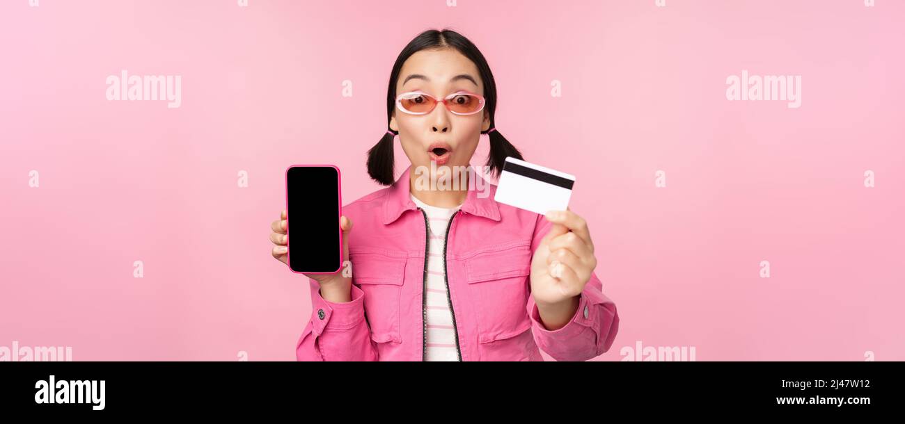 Asian girl shows mobile phone screen and credit card, reacts surprised ...
