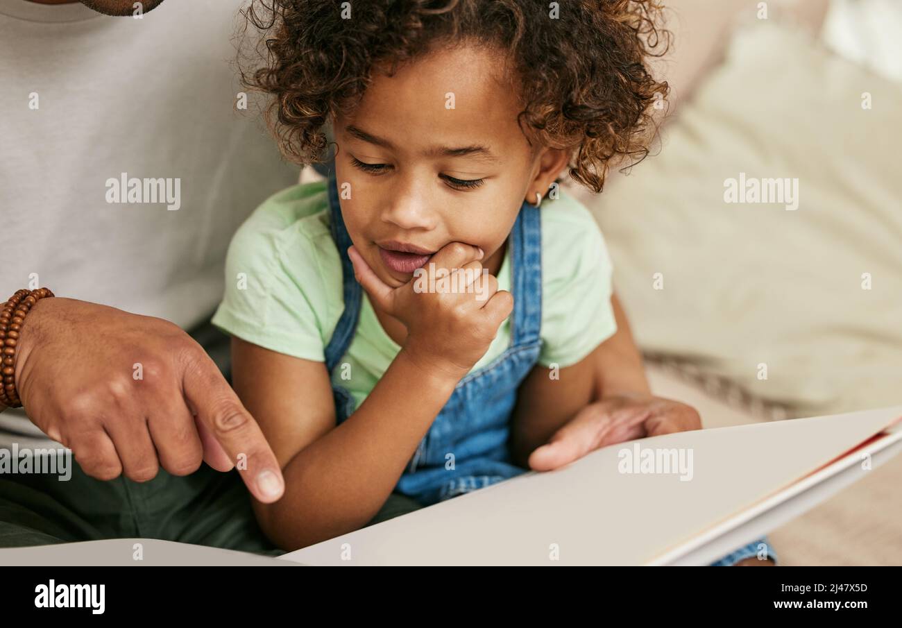 She loves this book. Shot of a little girl reading a book with her ...