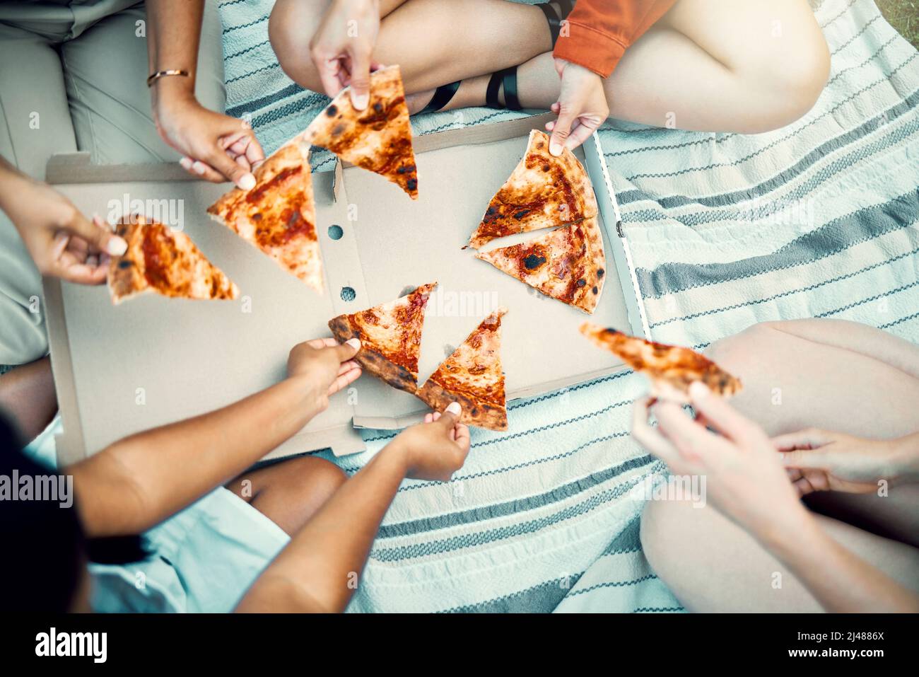 Chow time. Shot of an unrecognizable friends sharing pizza outside ...