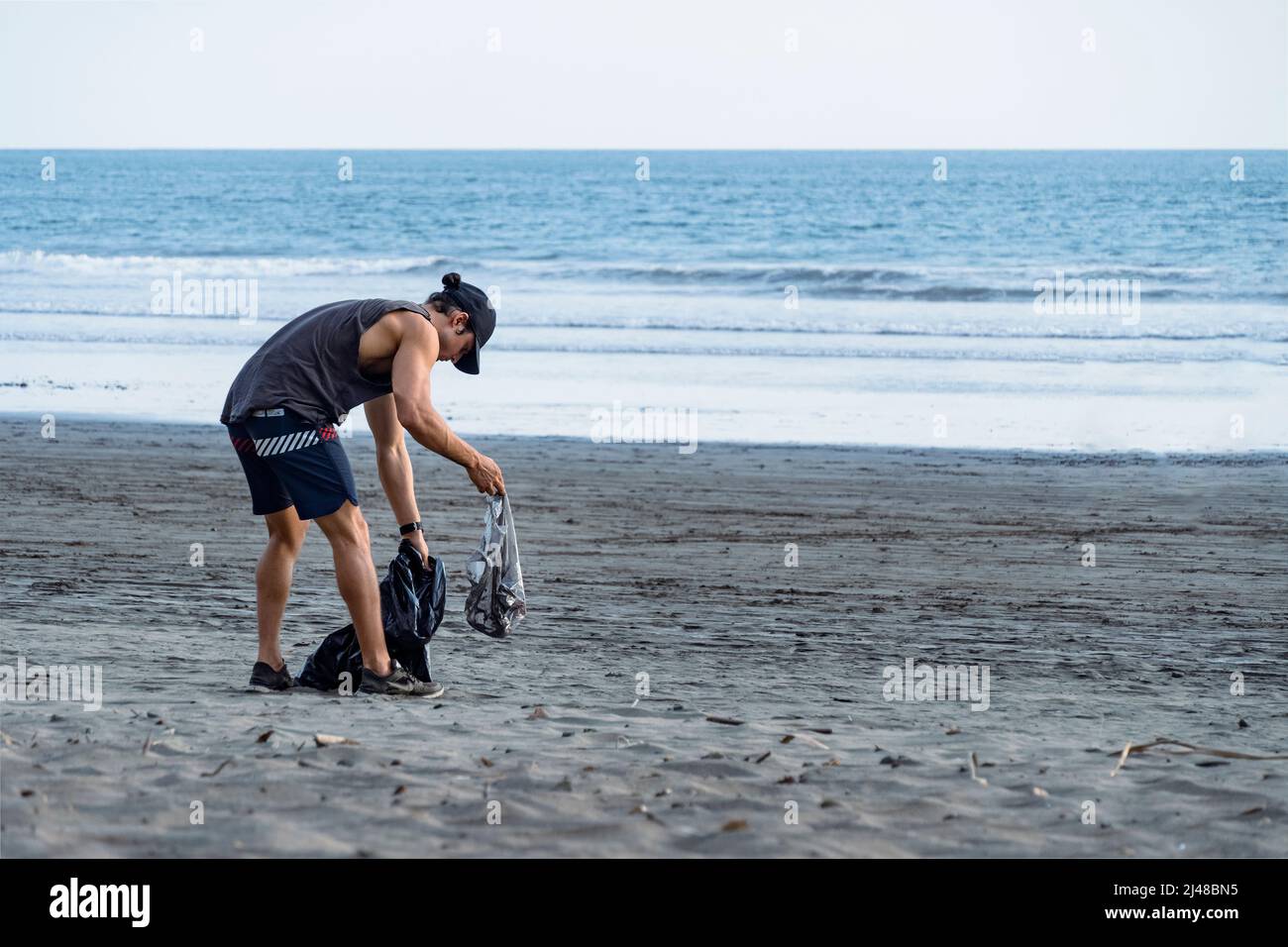 Young man picking up trash on the beach. Save the planet. Copy Space ...
