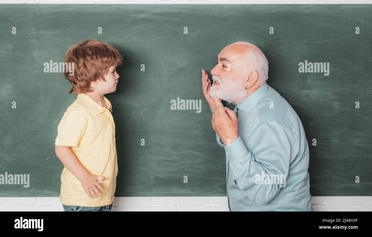 Teacher and schoolboy using computer in class over blackboard. Portrait ...