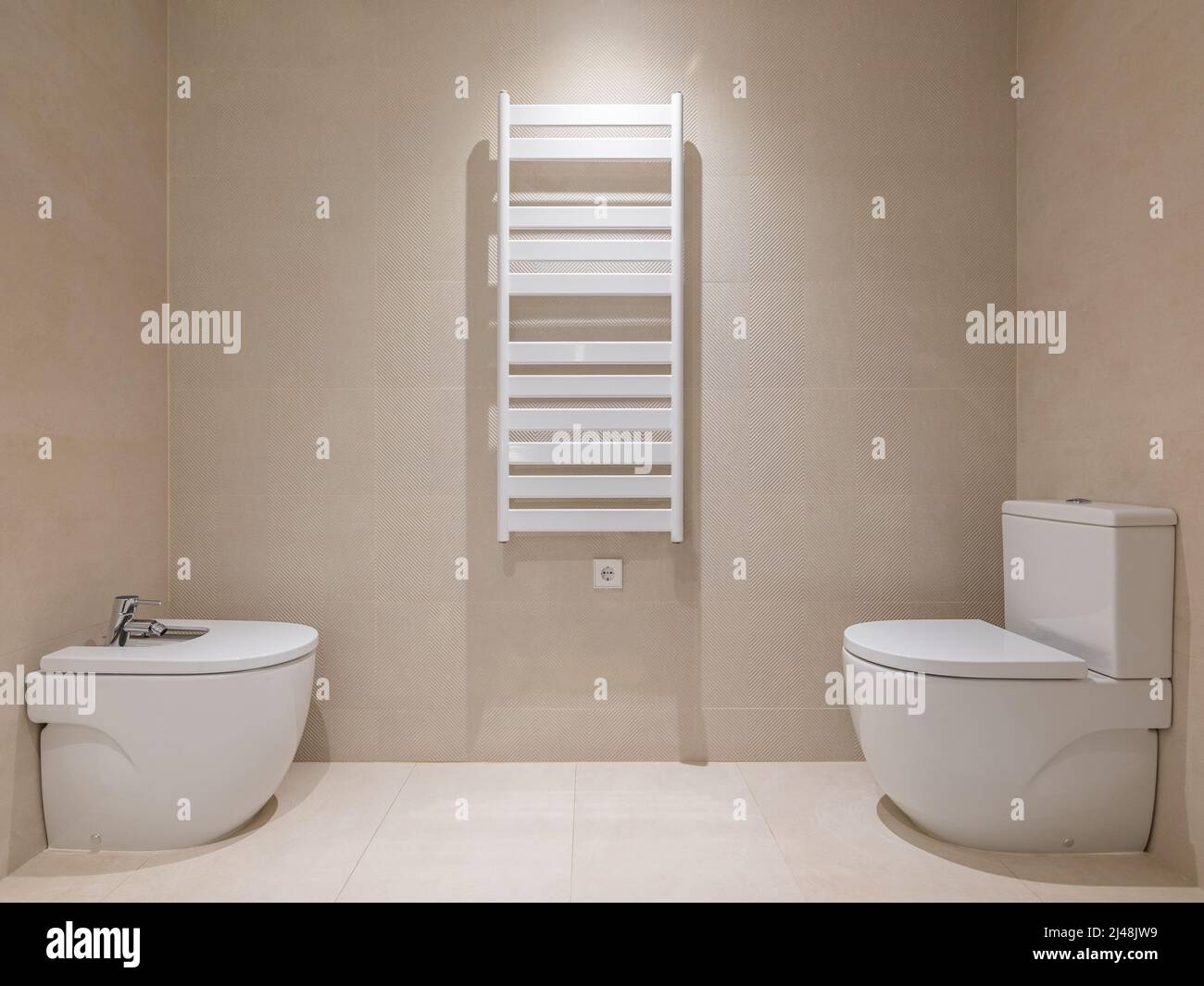 Toilet, bidet and heating radiator in a modern bathroom with beige ...