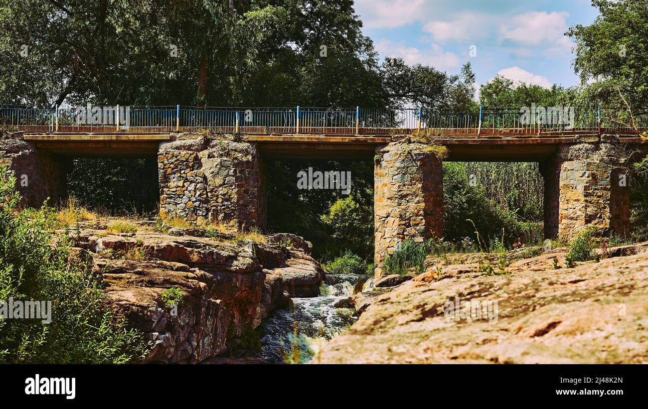 Old bridge in a Ukrainian village across a fast river with rocky shores ...