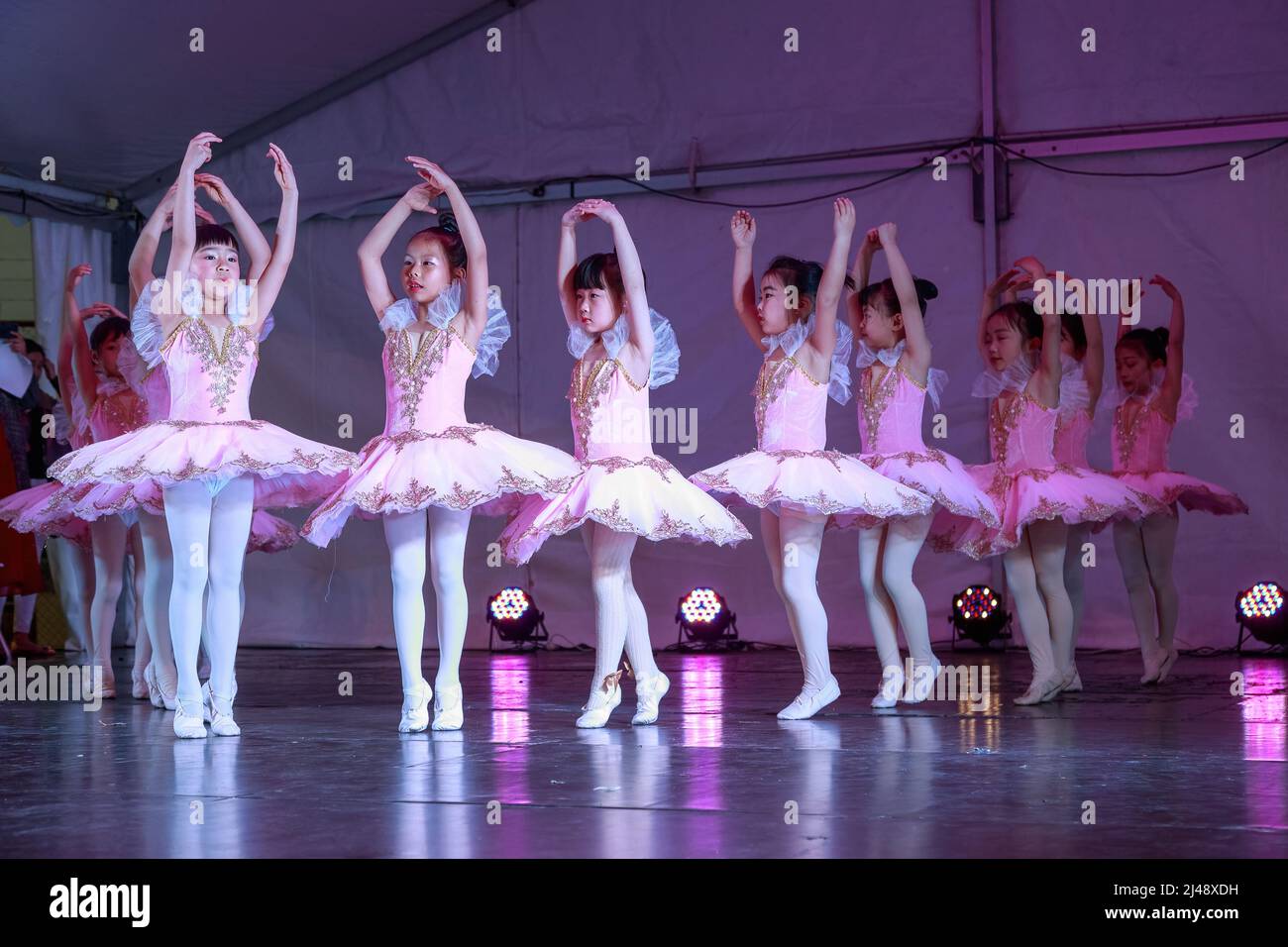 A group of young Asian ballerinas performing on stage in pink tutus ...