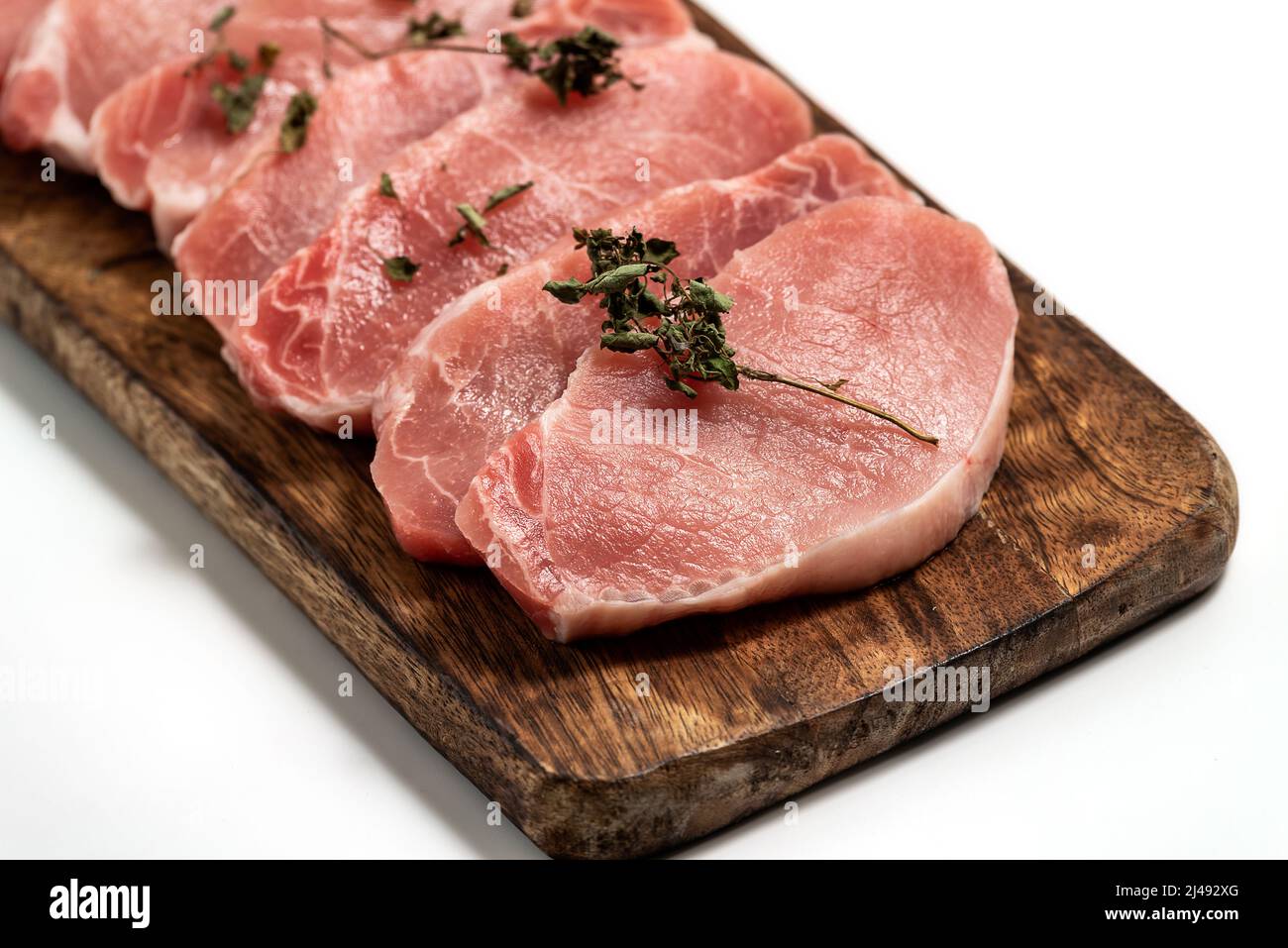 Raw pork sliced meat on wooden board on white background with dry basil ...