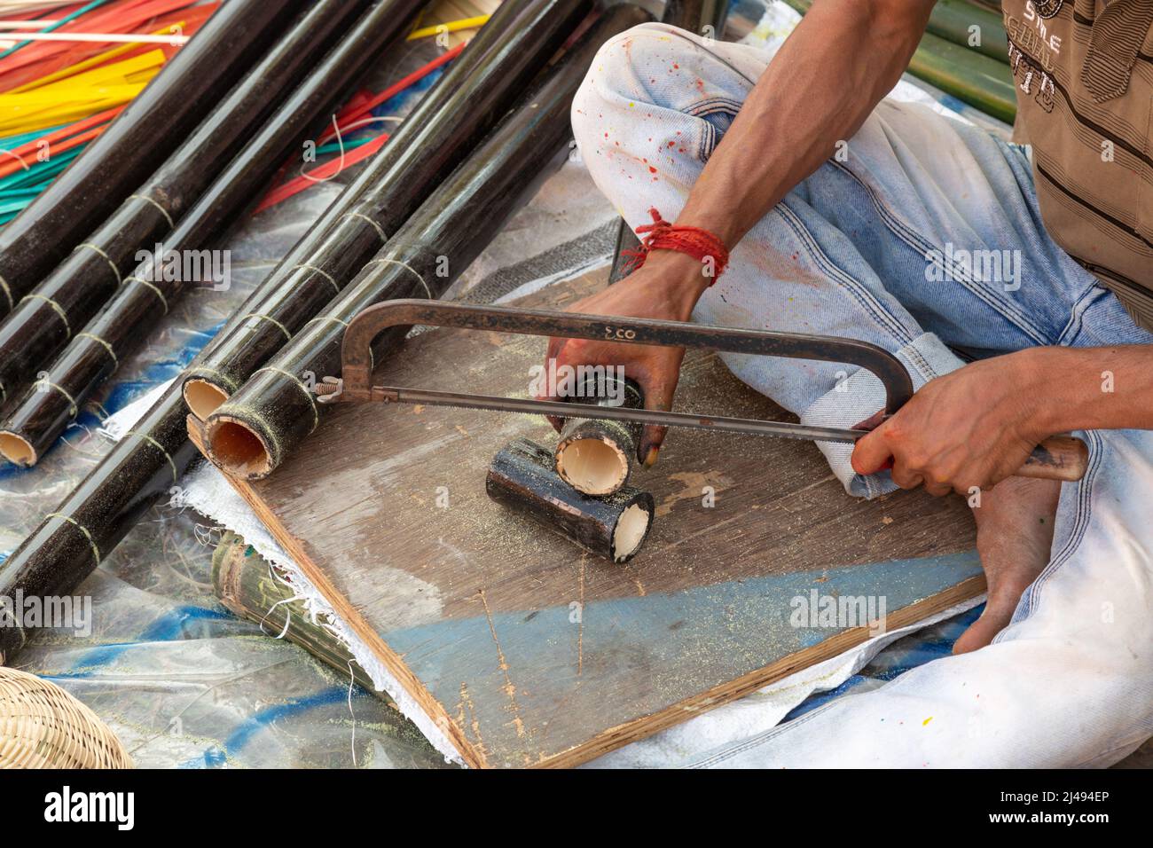 Local craftsman cutting bamboo poles with a saw for making craft items ...