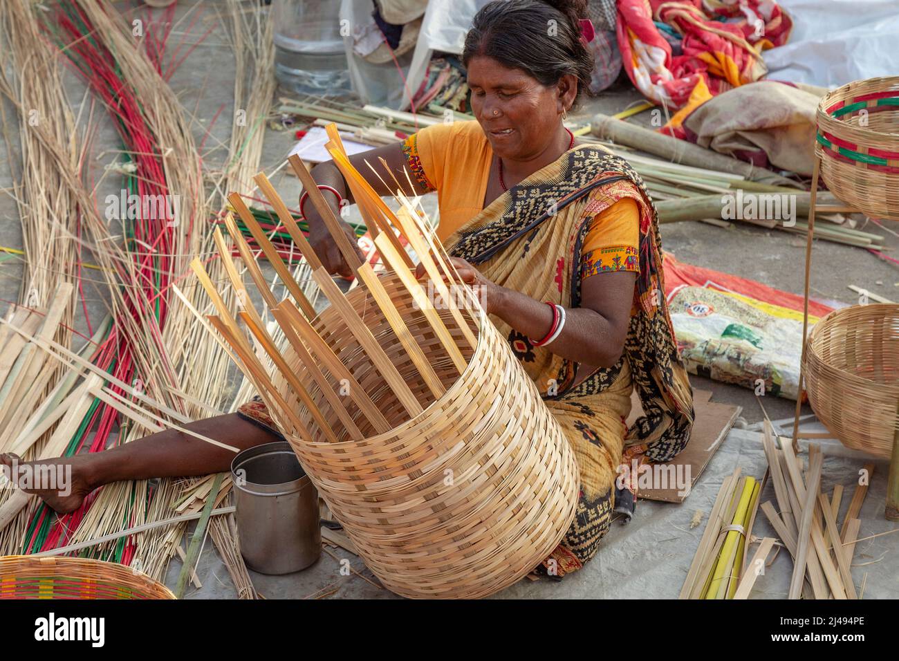 Rural Indian woman weaving a basket with bamboo straws for sale at a ...
