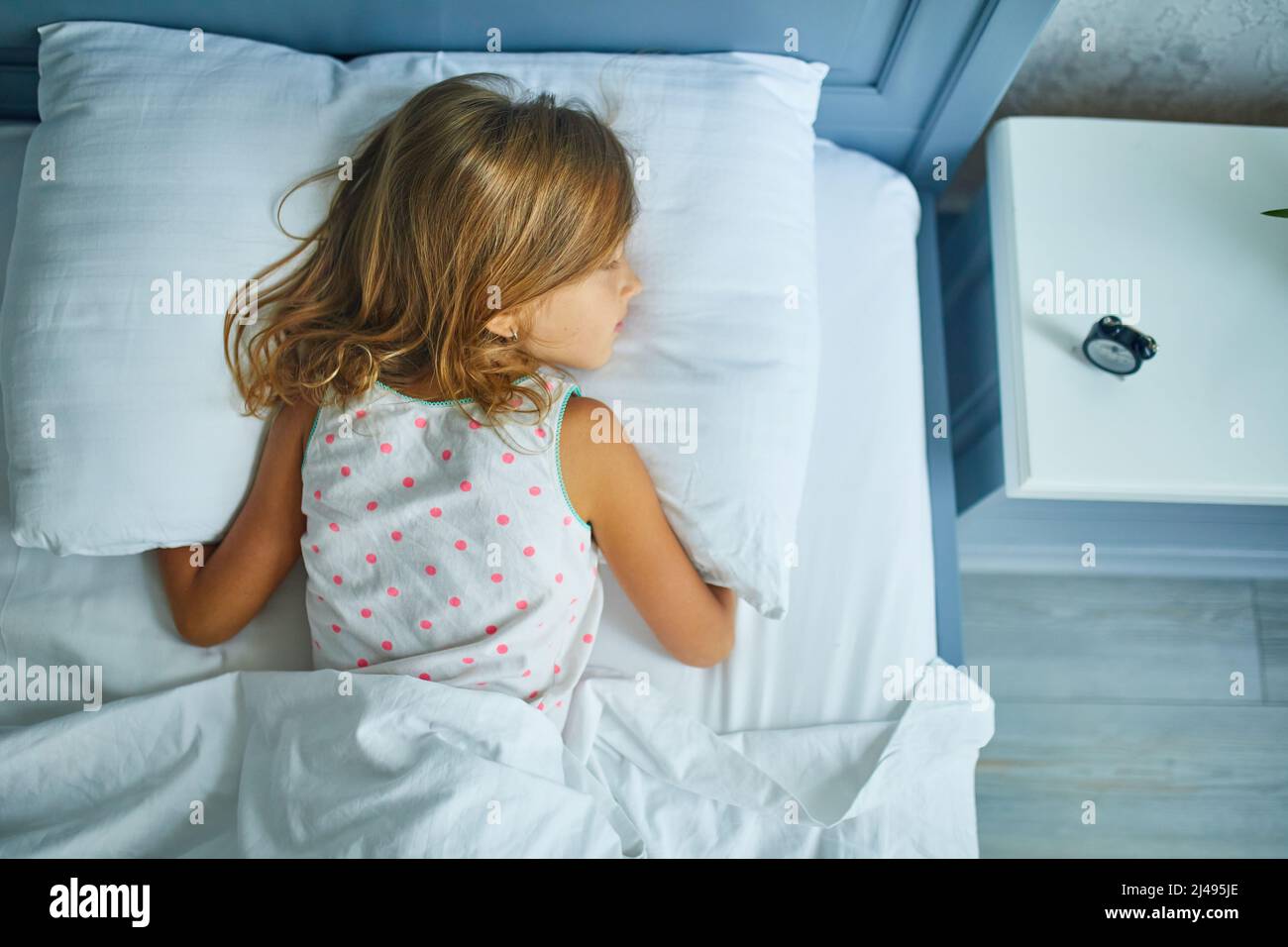 Little girl sleeping on a big and cozy bed white linen in the afternoon ...