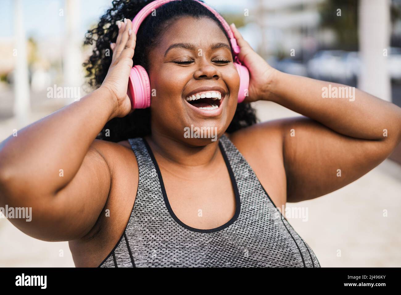 Curvy woman dancing and listening music with headphones while jogging ...