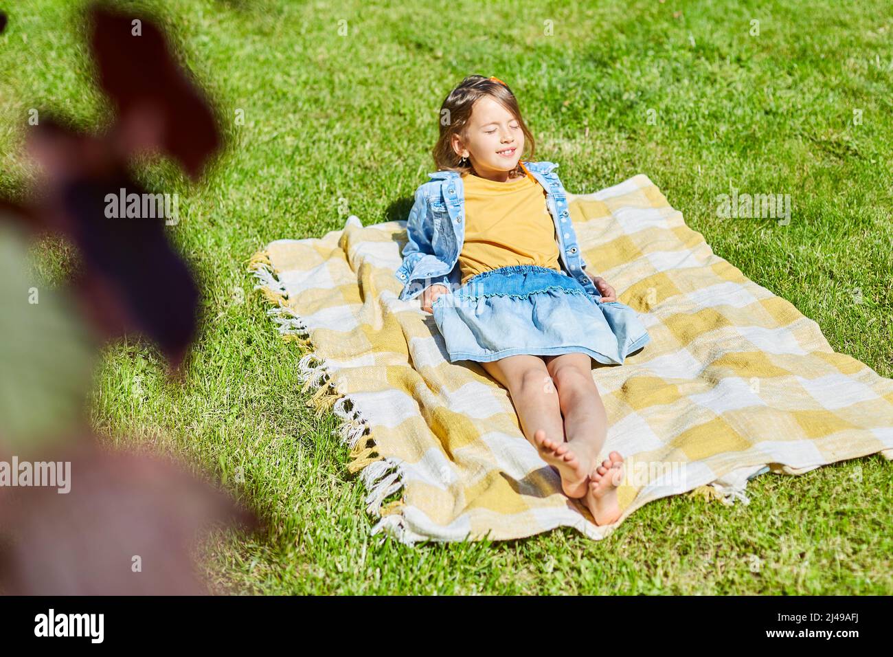 Child lying on the blanket, on the grass in the sun day, little girl take sunbathes on backyard ...