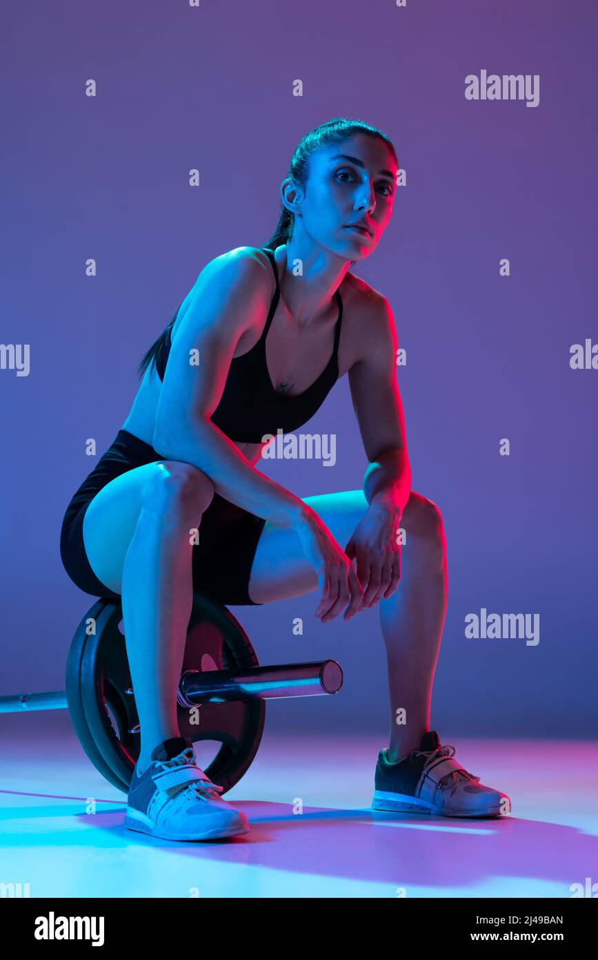 Studio shot of female athlete, sportive woman posing with barbell ...